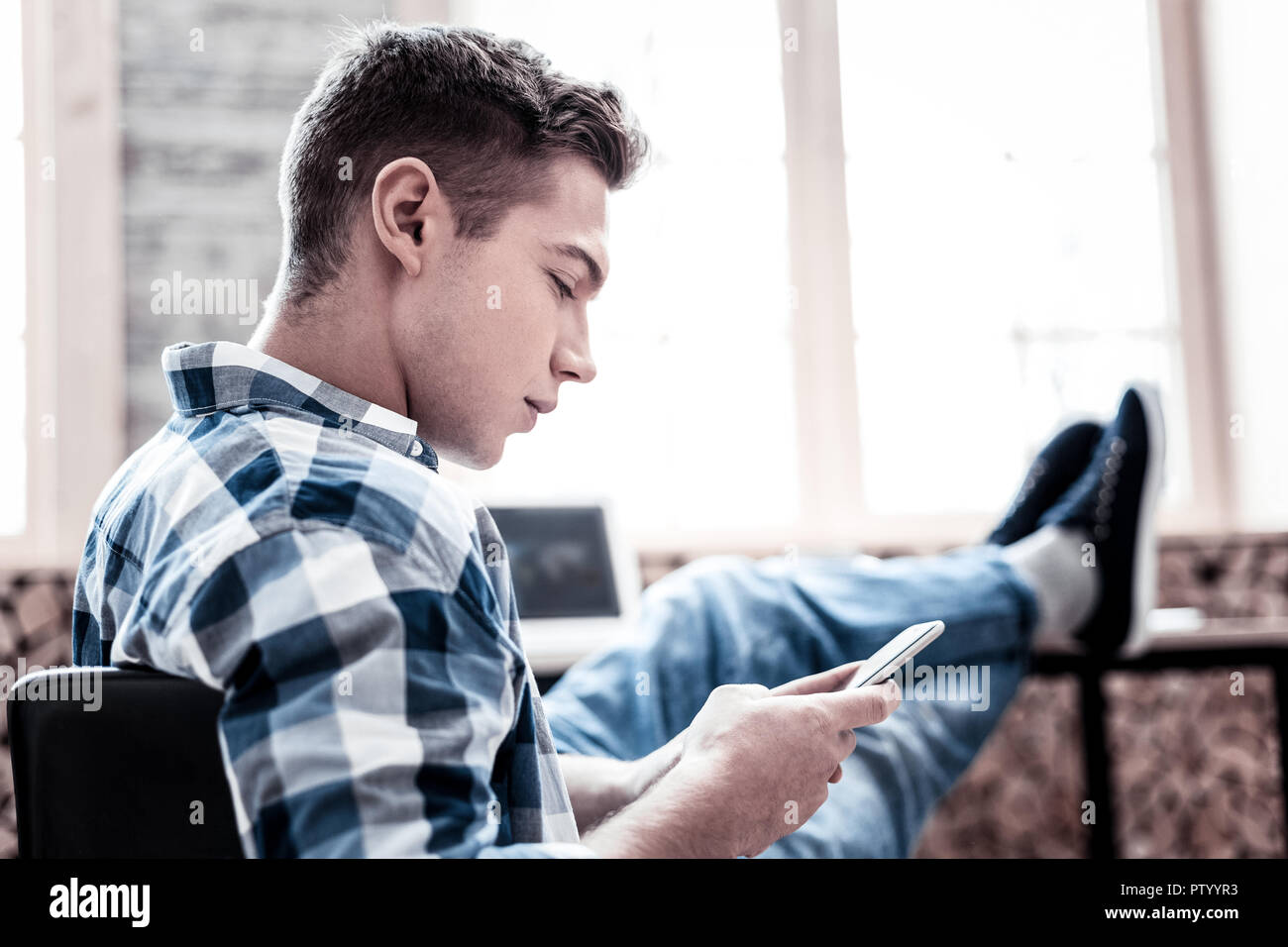 Calm person sitting at home and reading messages in his smartphone ...