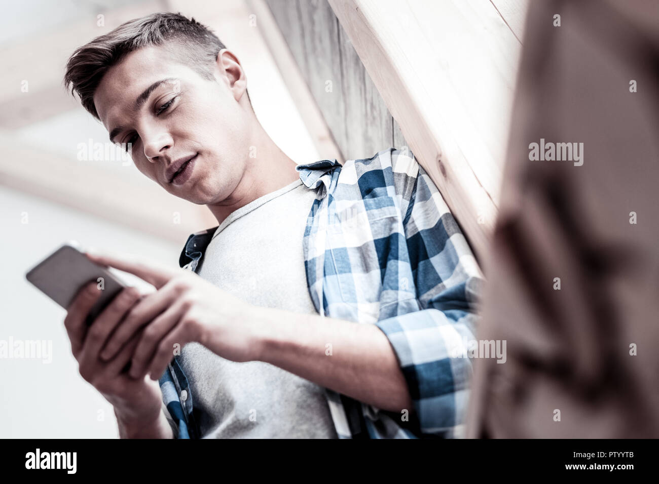 Calm young man typing messages while standing by the window Stock Photo ...