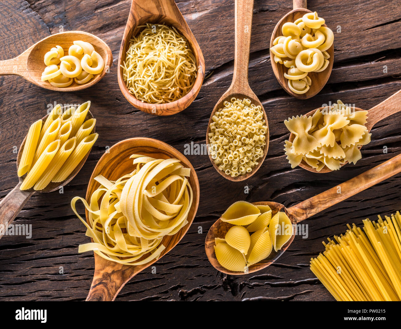 Different pasta types in wooden spoons on the table. Top view Stock ...