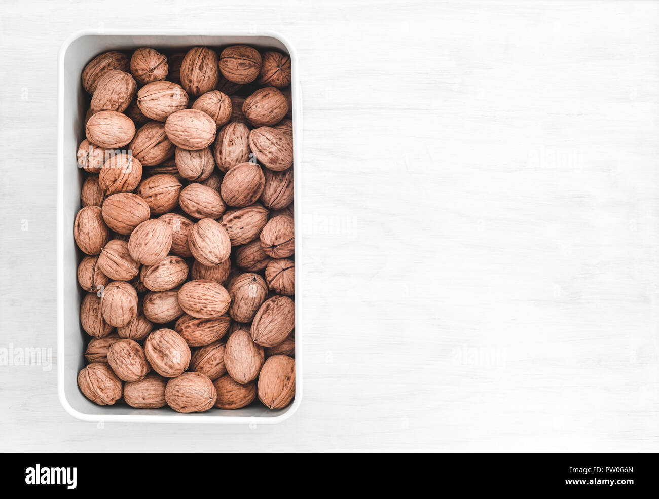 Box full of walnuts, on white painted wooden background with copy space ...