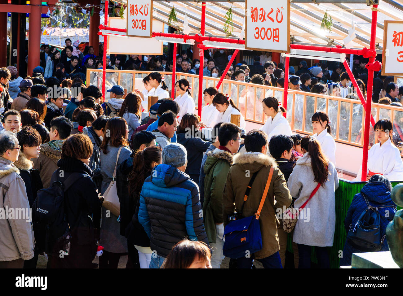 Japanese new year, shogatsu. Shrine Maidens, Miko, at busy counter selling Omikuji paper fortune ...