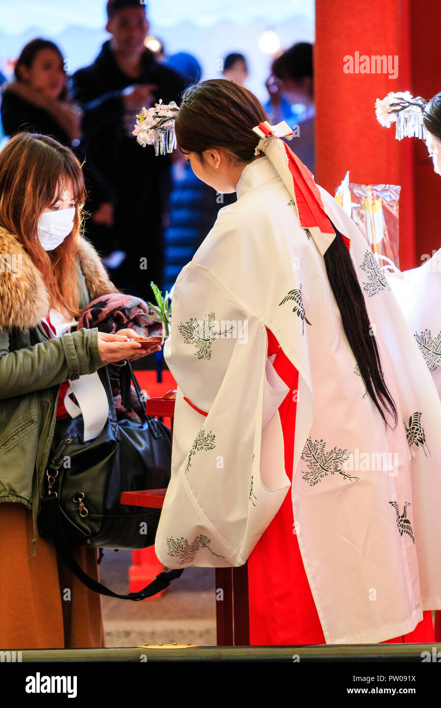 Japanese new year, shogatsu. Shrine Maiden, Miko, hands a woman a cup ...