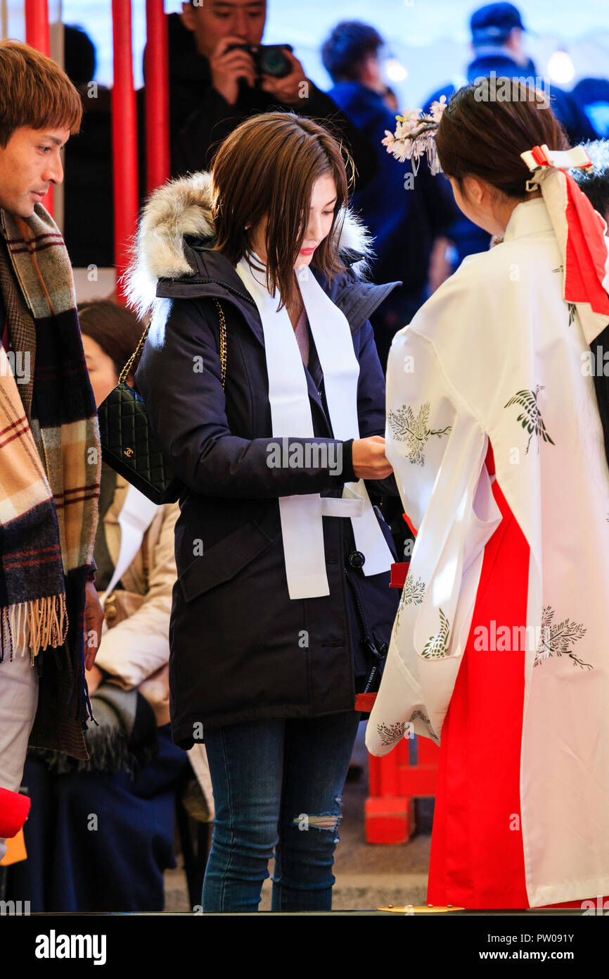 Japanese new year, shogatsu. Shrine Maiden, Miko, hands a woman a cup ...