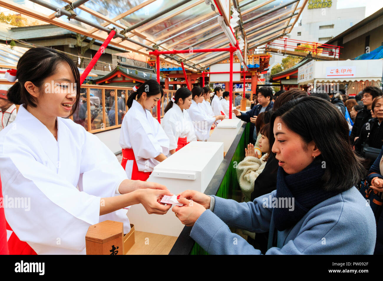 Japanese new year, shogatsu. Shrine Maidens, Miko, at busy counter selling Omikuji paper fortune ...