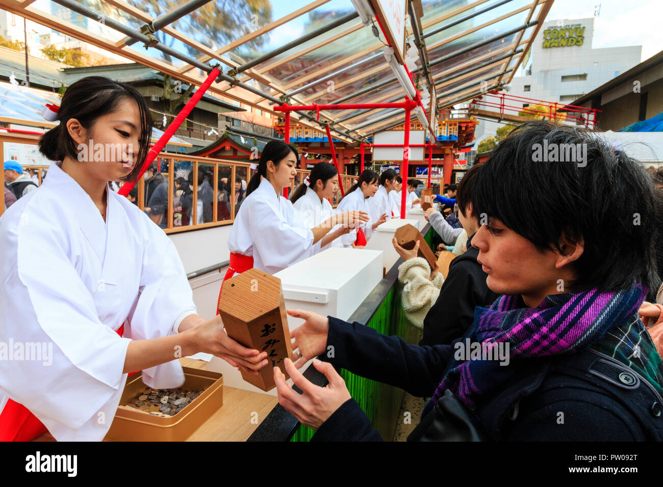 Japanese new year, shogatsu. Shrine Maidens, Miko, at busy counter selling Omikuji paper fortune ...