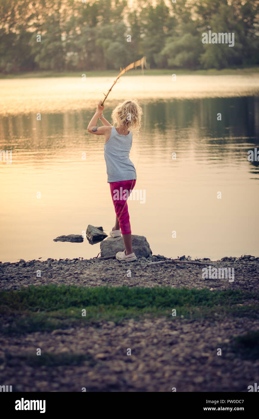 adorable little girl fishing with home made fishing rod at the pond at ...