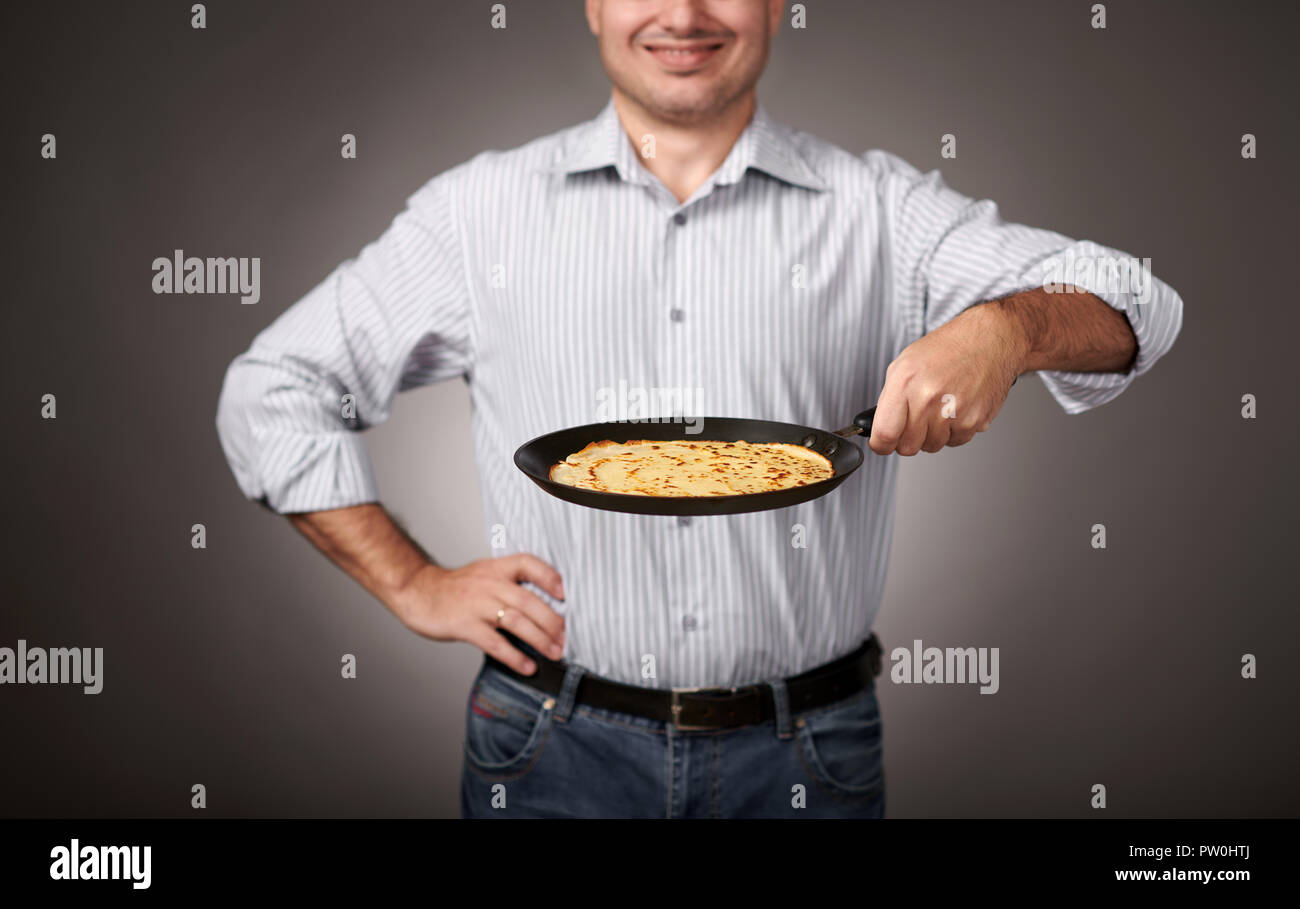 man posing with a pancake in a pan, white shirt and pants, gray ...