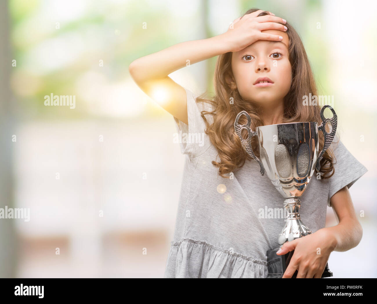 Brunette hispanic girl holding a trophy stressed with hand on head ...
