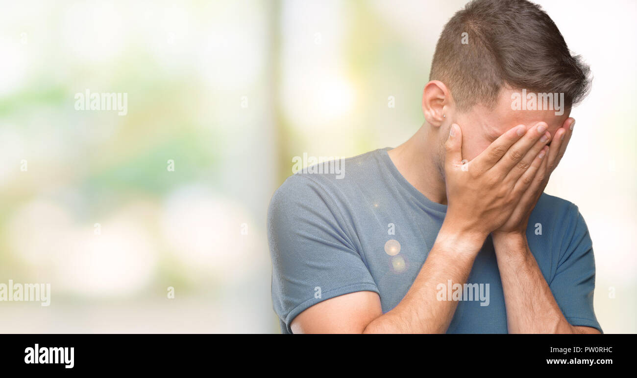 Handsome young casual man with sad expression covering face with hands ...