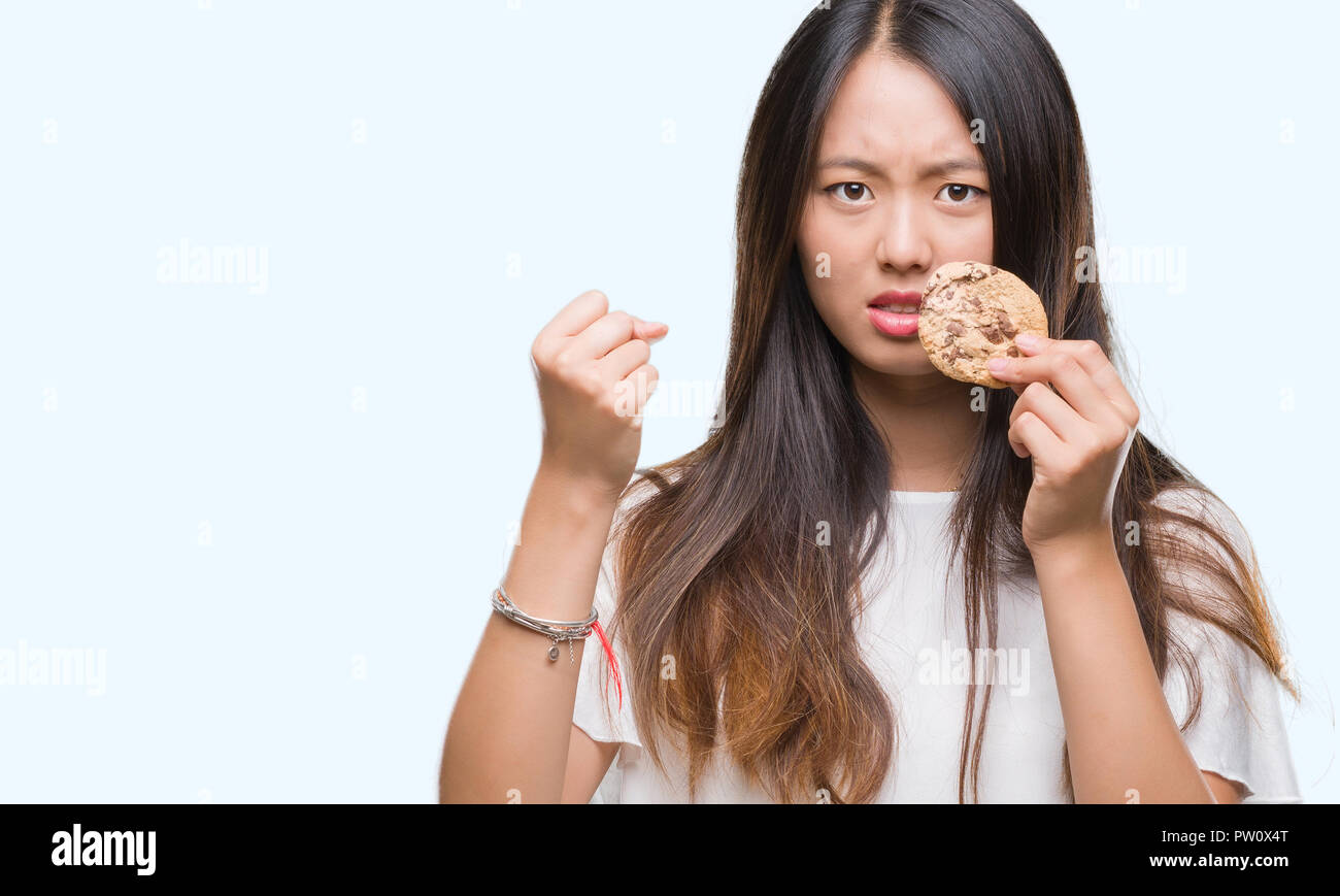 Young asian woman eating chocolate chip cookie over isolated background ...