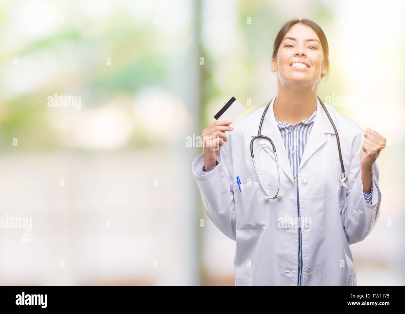 Young hispanic doctor woman holding credit card screaming proud and ...