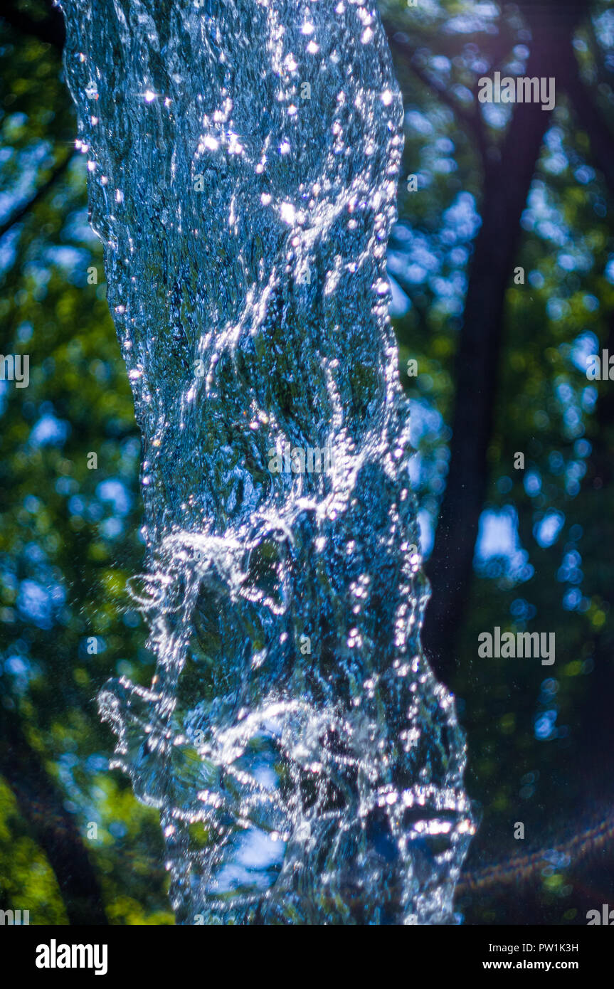 transparent falling water vertical flows against a blue sky and green ...