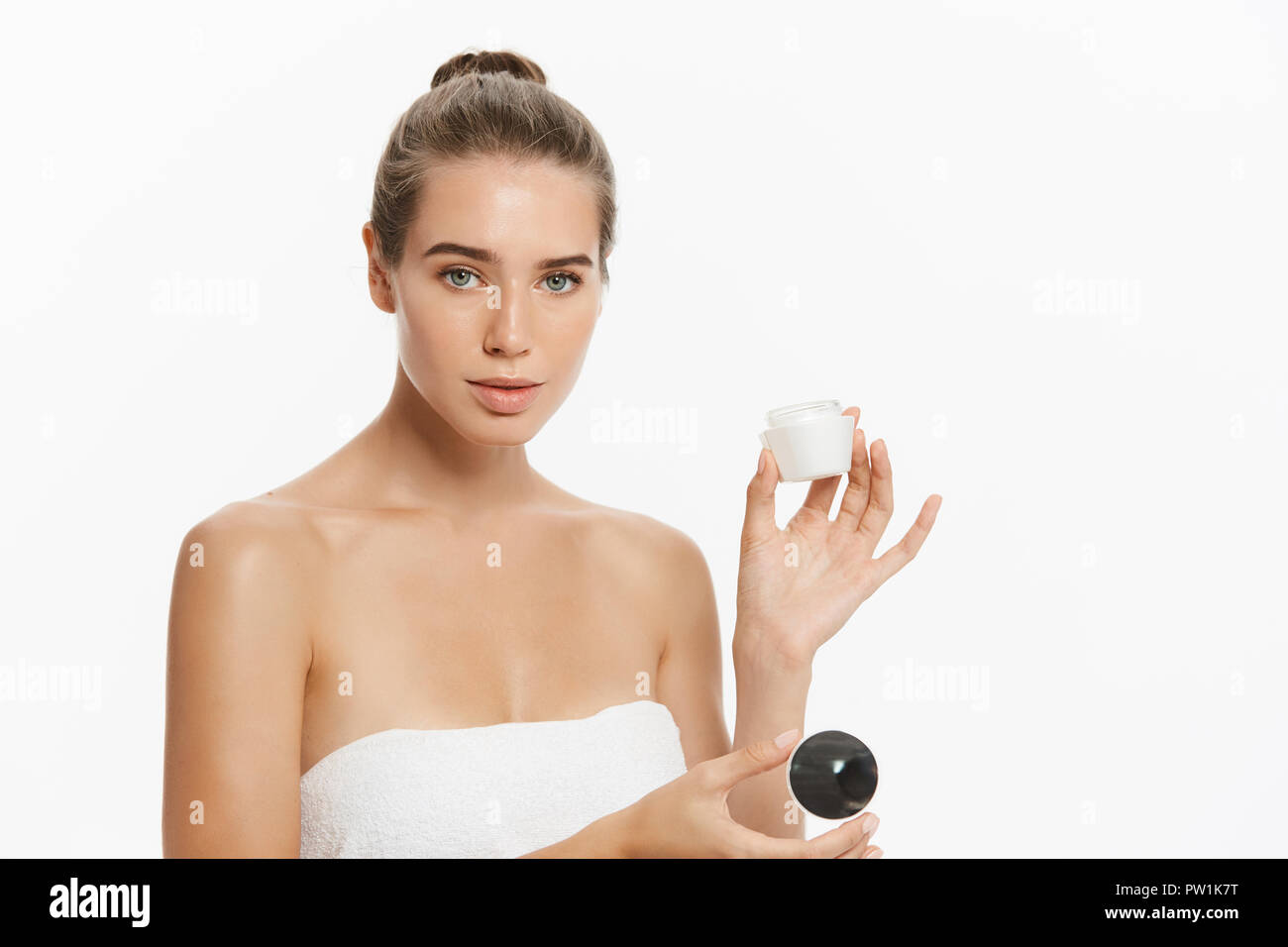 Beautiful young woman applying cosmetic cream treatment on her face isolated on white background ...