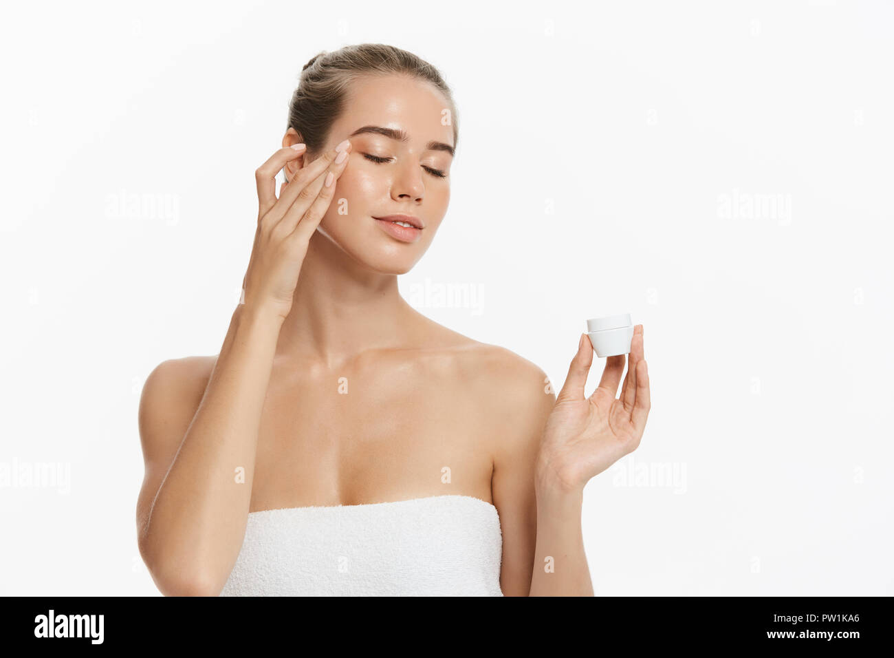 Beautiful young woman applying cosmetic cream treatment on her face isolated on white background ...