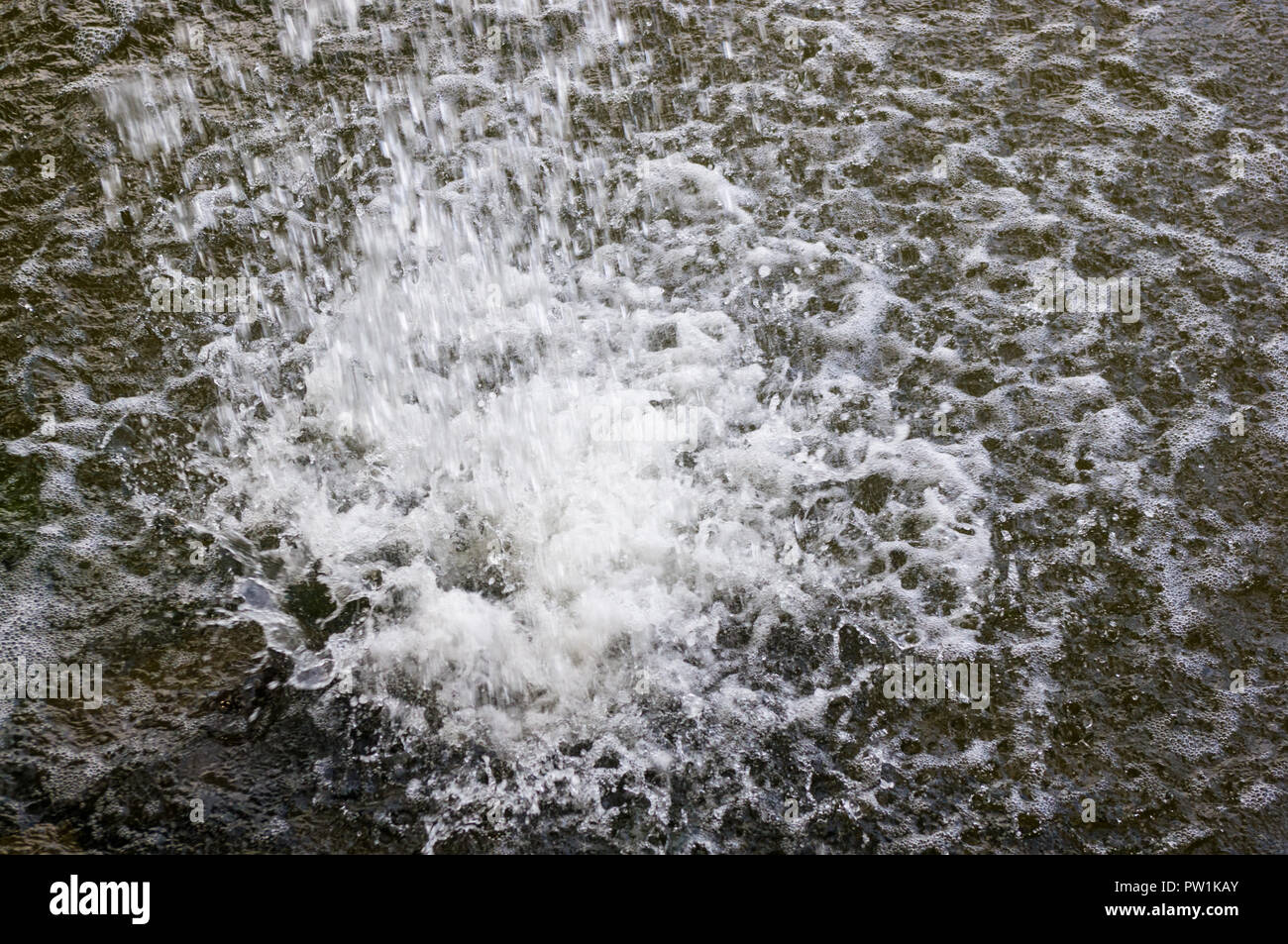 transparent falling water vertical flows against a blue sky and green ...