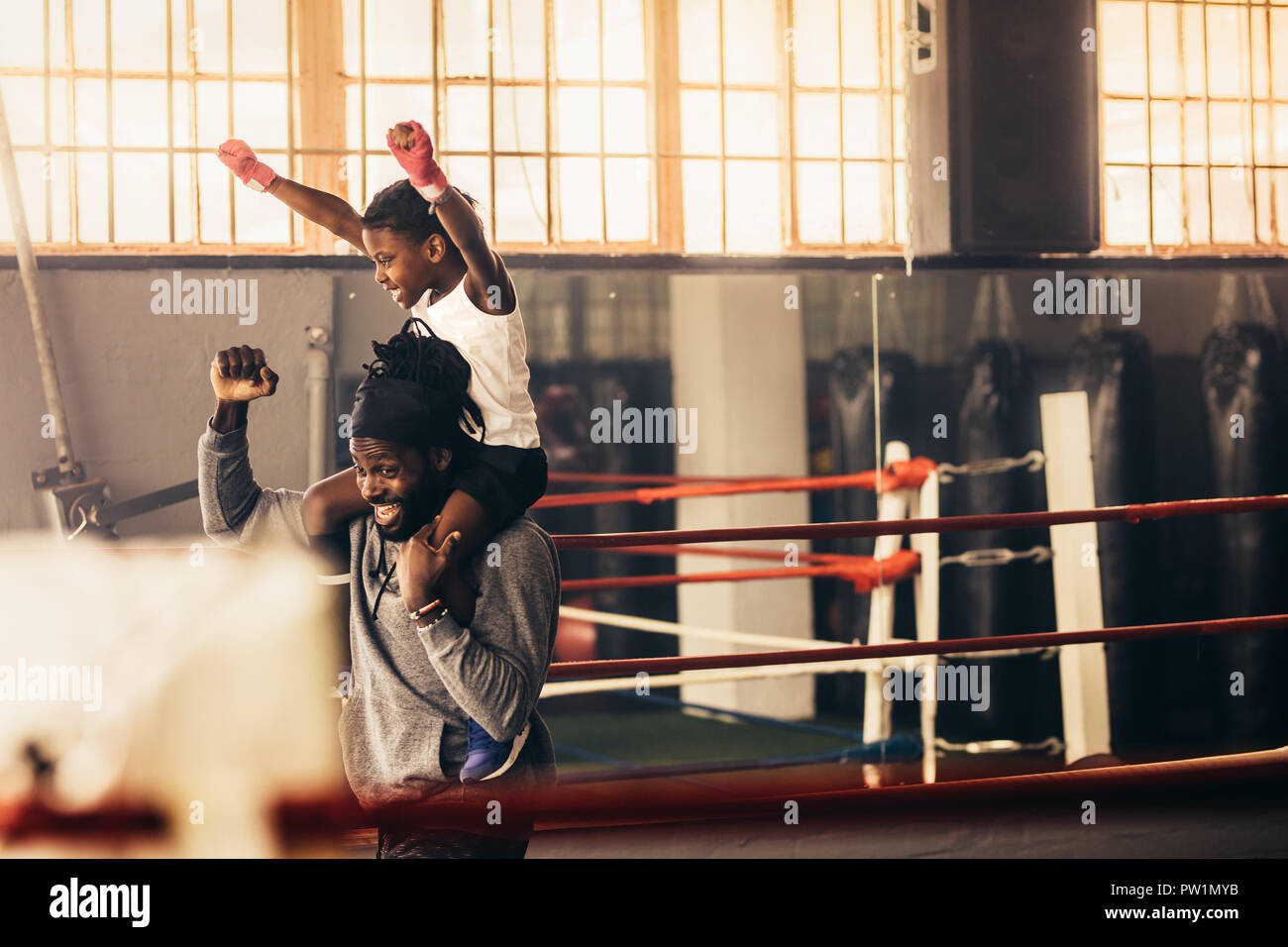 Coach carrying a boxing kid on his shoulders walking in the gym ...