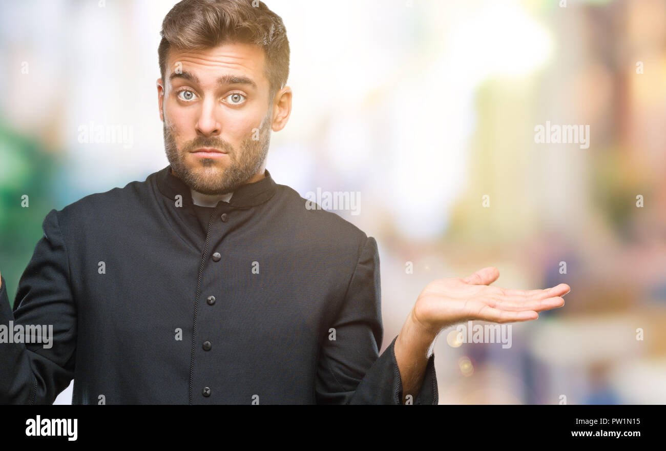 Young catholic christian priest man over isolated background clueless ...