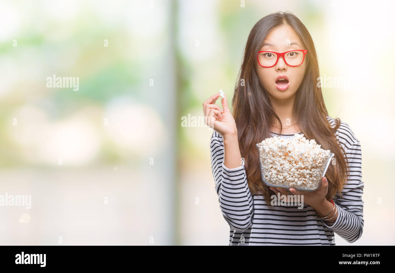 Young asian woman eating popcorn over isolated background scared in ...