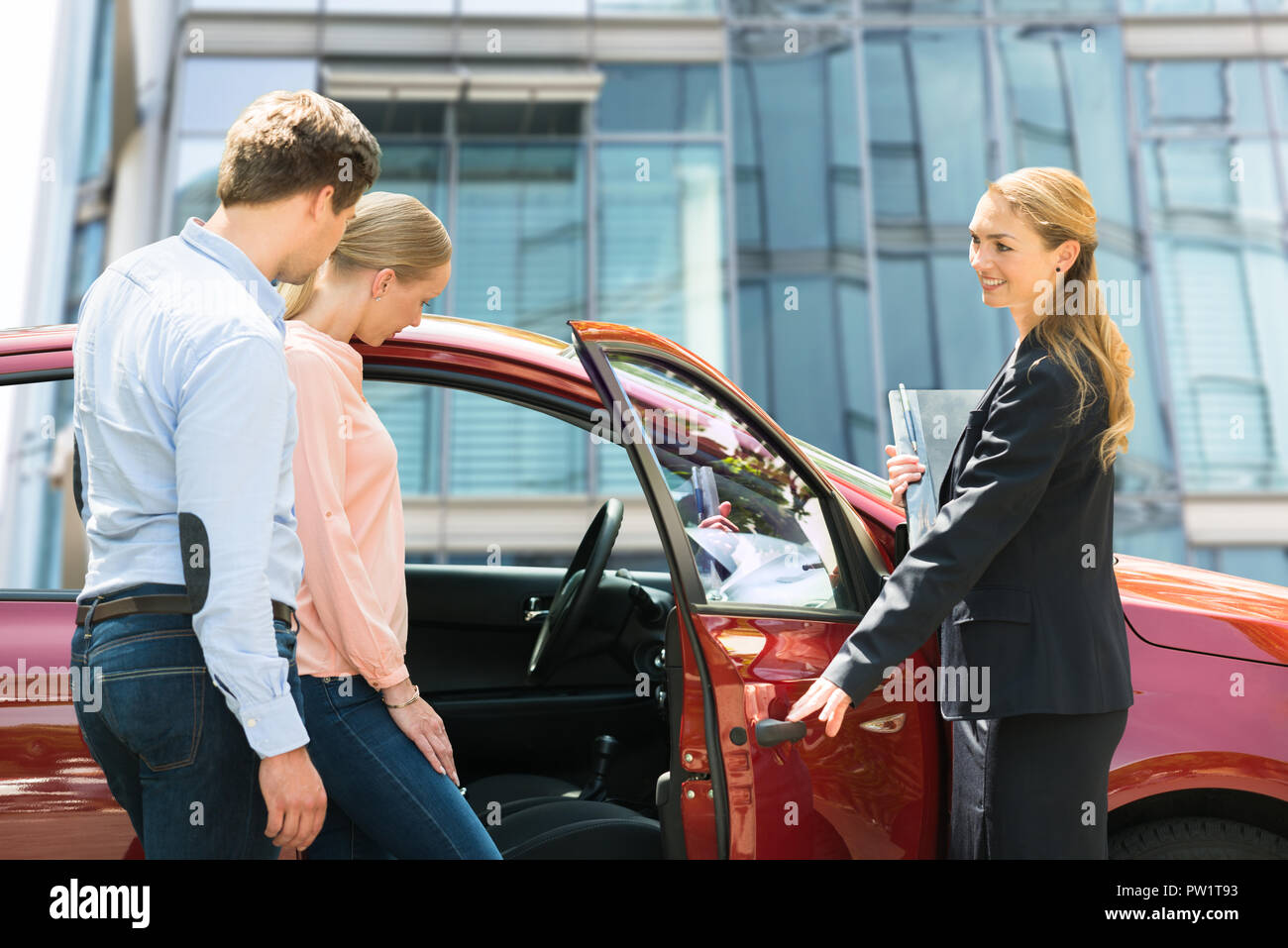 Smiling Female Dealer Opening Red Car Door For Young Couple Stock Photo ...