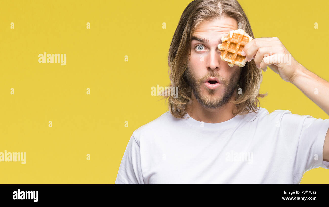 Young handsome man with long hair over isolated background eating ...