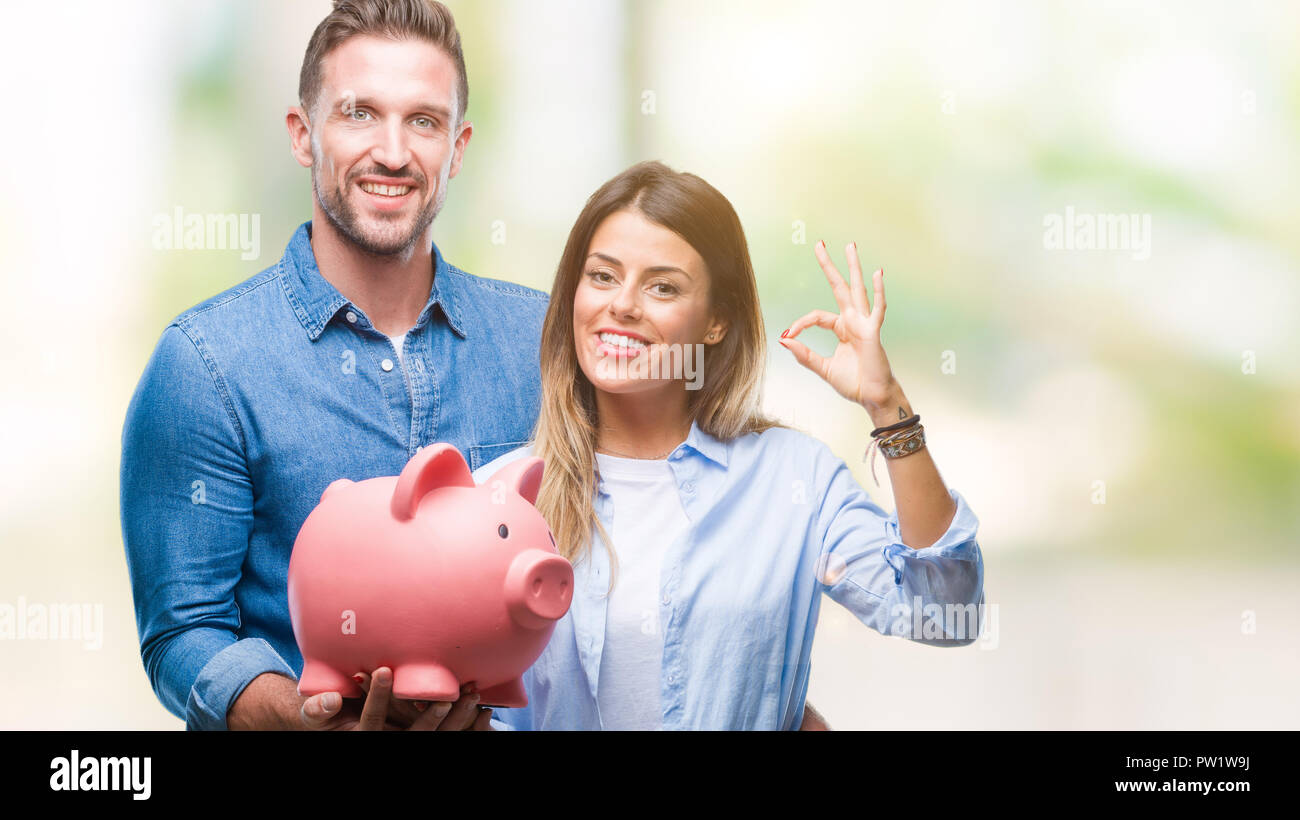 Young couple in love holding piggy bank over isolated background doing ...