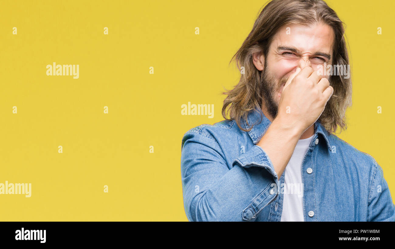 Young handsome man with long hair over isolated background smelling ...