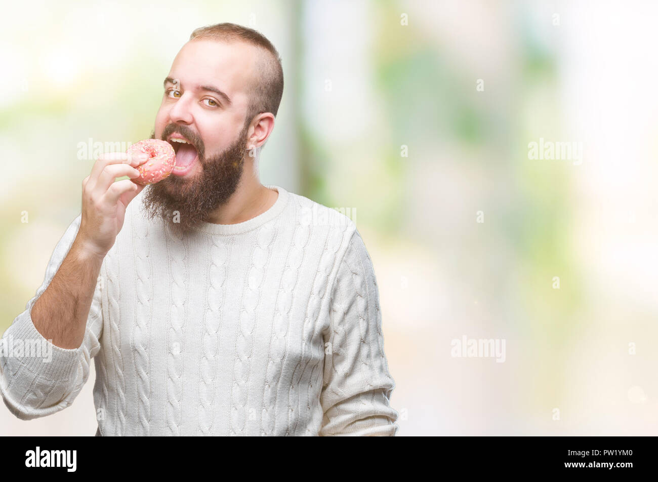 Young caucasian hipster man eating sweet donut over isolated background ...