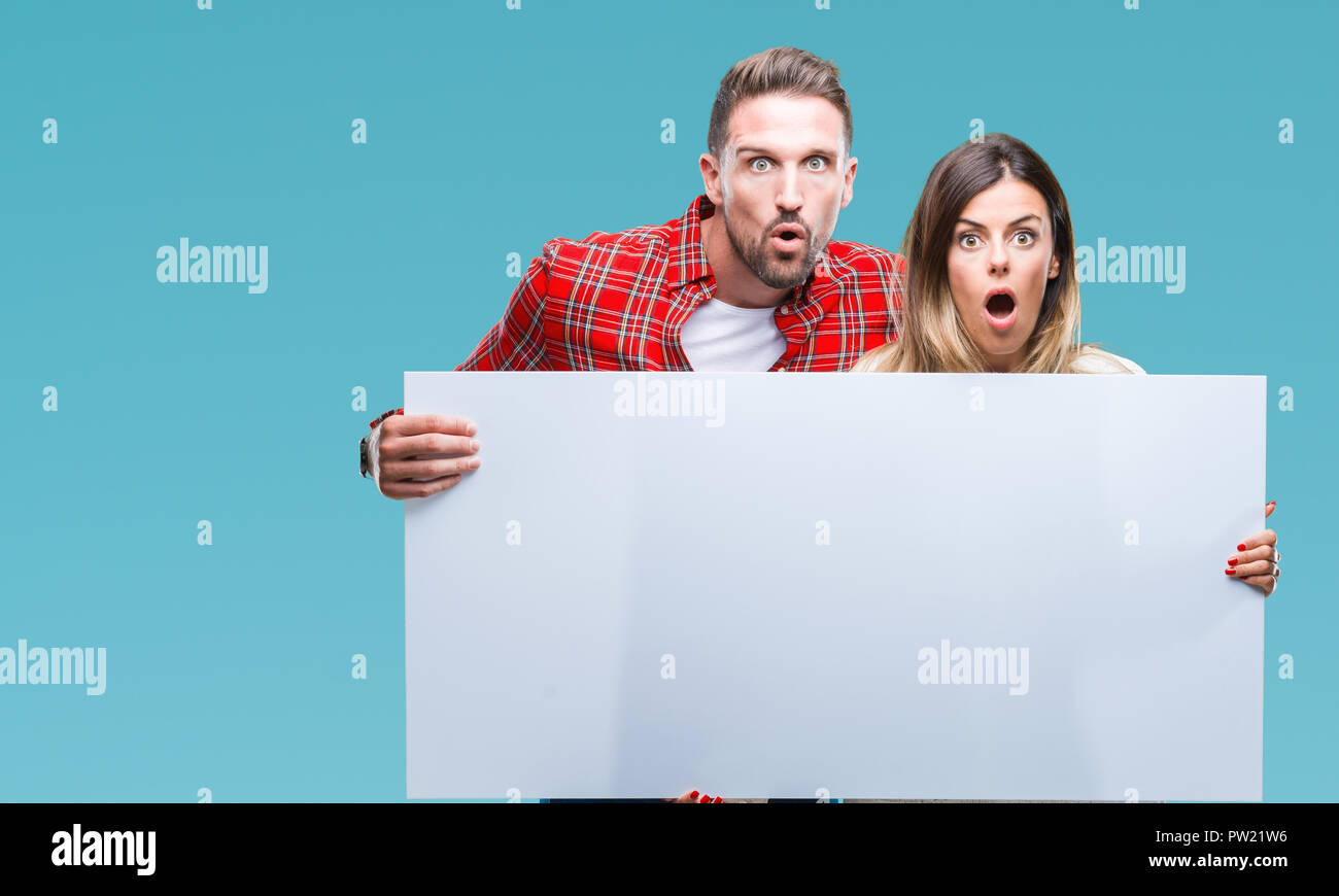 Young couple together holding blank banner over isolated background ...