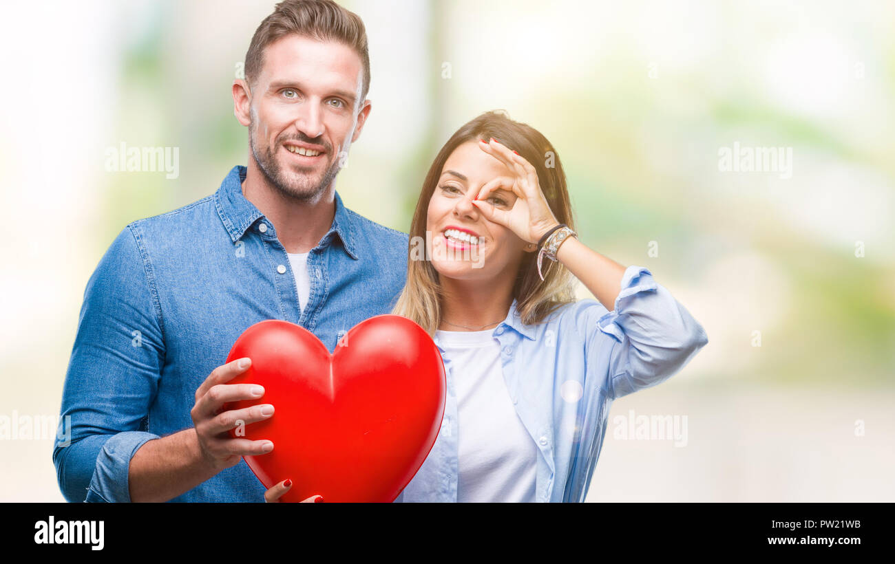Young couple in love holding red heart over isolated background with ...