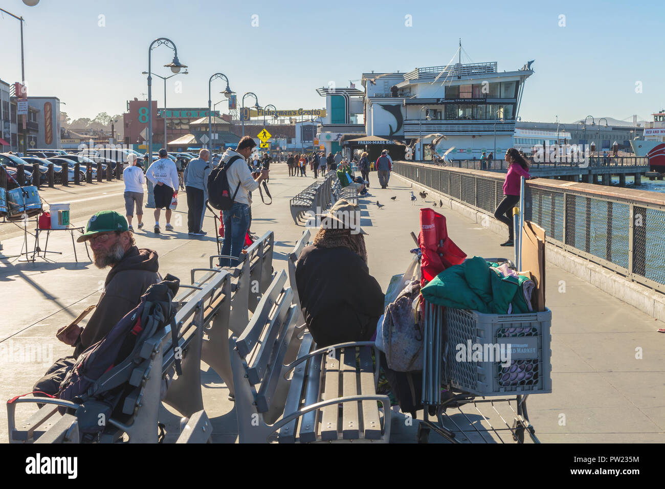 Two homeless men sit on the benches at Fisherman's Wharf, with tourists ...
