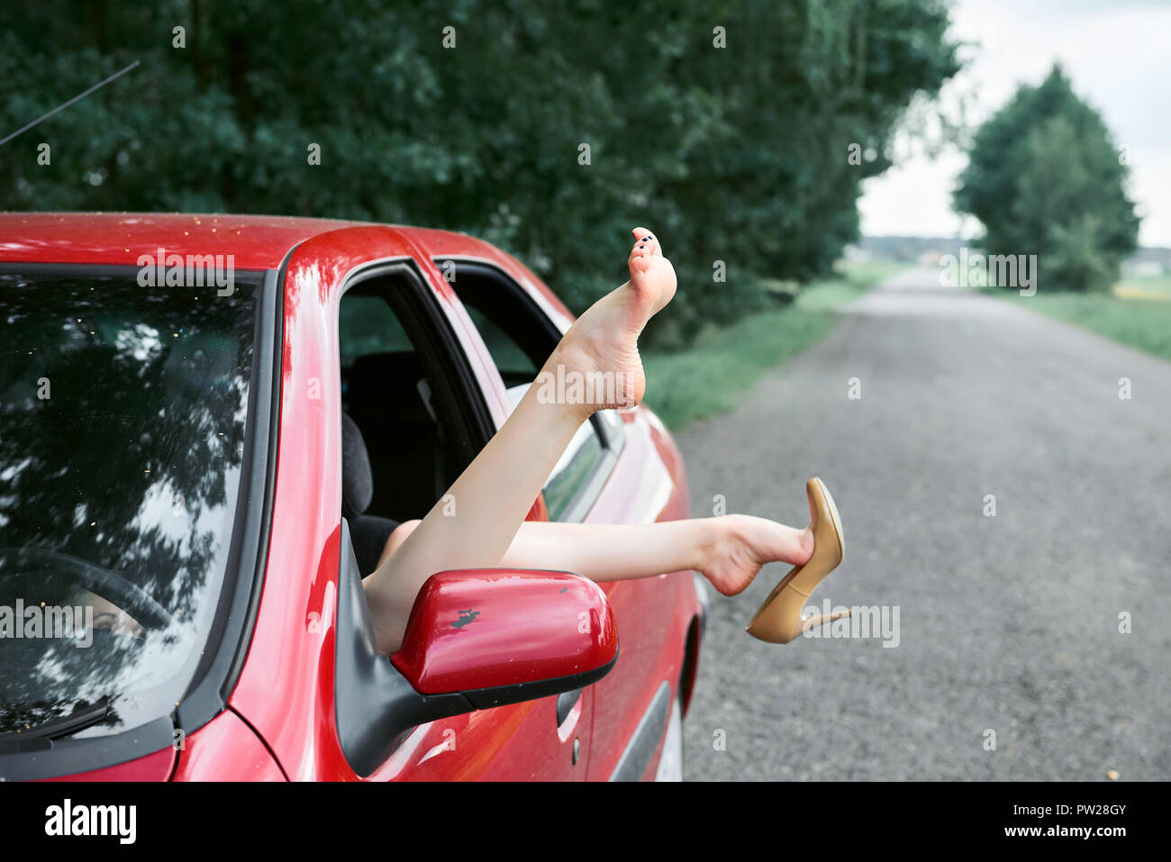 young woman driver resting in a red car, put her feet on the car window ...