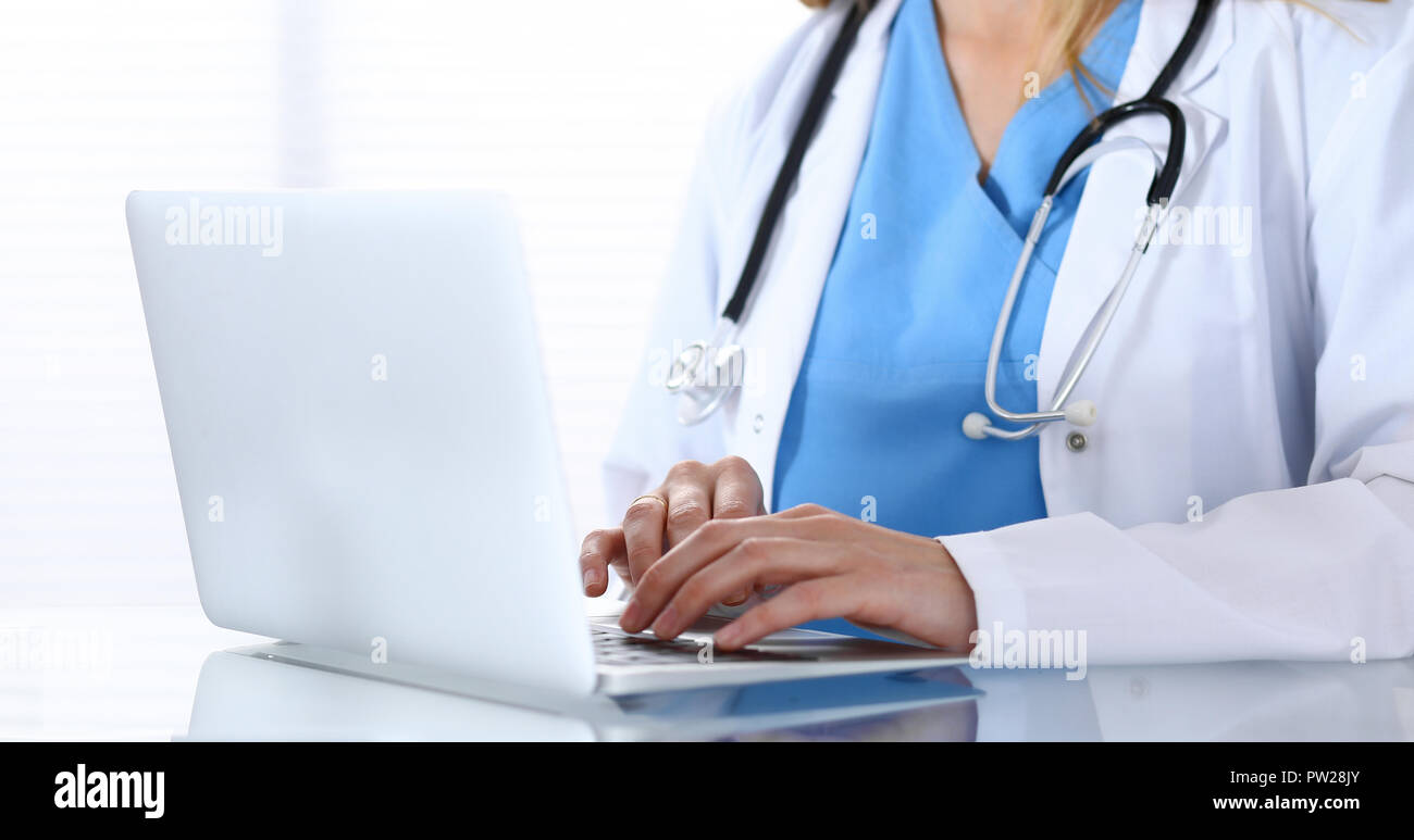 Doctor typing on laptop computer while sitting at the glass desk in ...