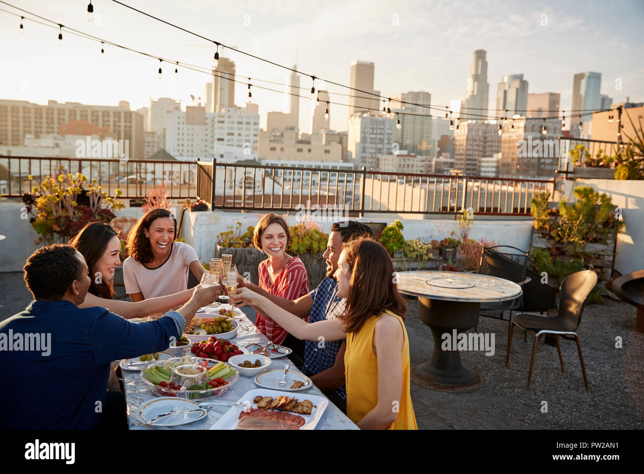 Friends Gathered On Rooftop Terrace For Meal With City Skyline In ...
