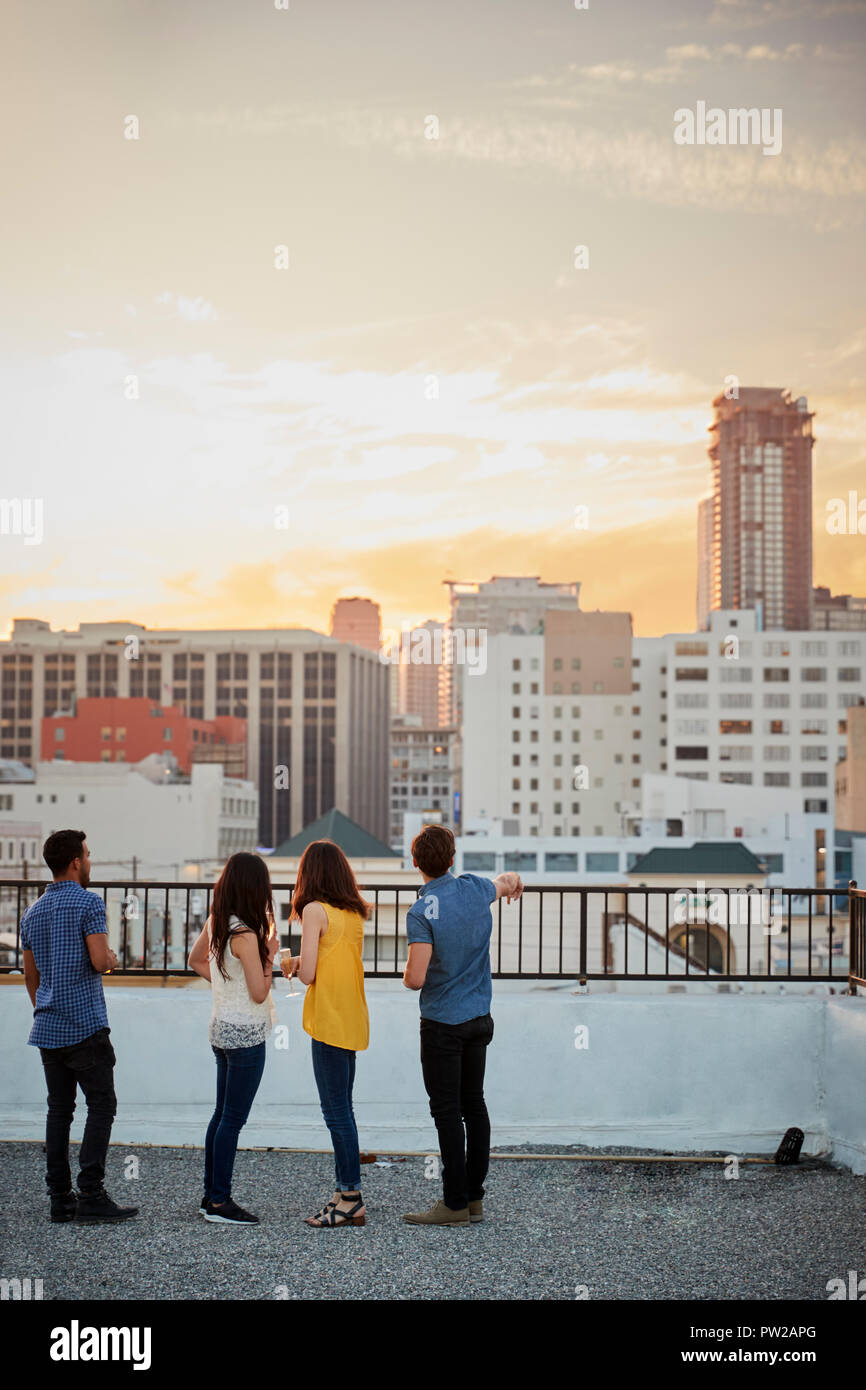 Rear View Of Friends On Rooftop Terrace Looking Out Over City Skyline ...
