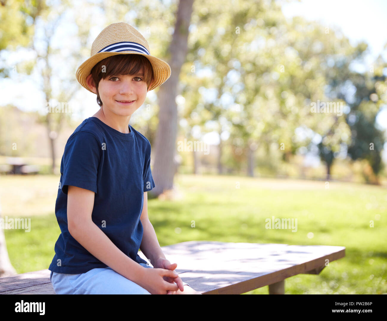 Young schoolboy in hat sits on park bench smiling to camera Stock Photo ...