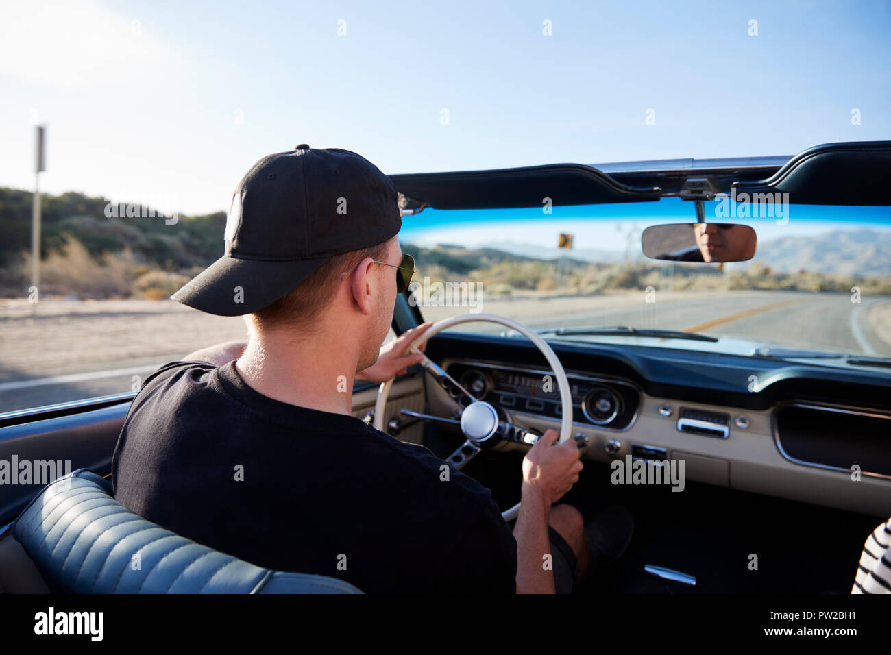 Rear View Of Man On Road Trip Driving Classic Convertible Car Towards ...
