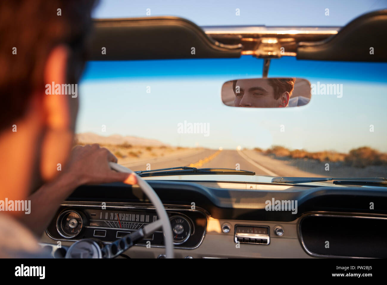 Rear View Of Man On Road Trip Driving Classic Convertible Car Towards ...