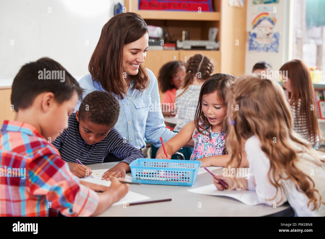 Teacher sitting at table with young school kids in lesson Stock Photo ...