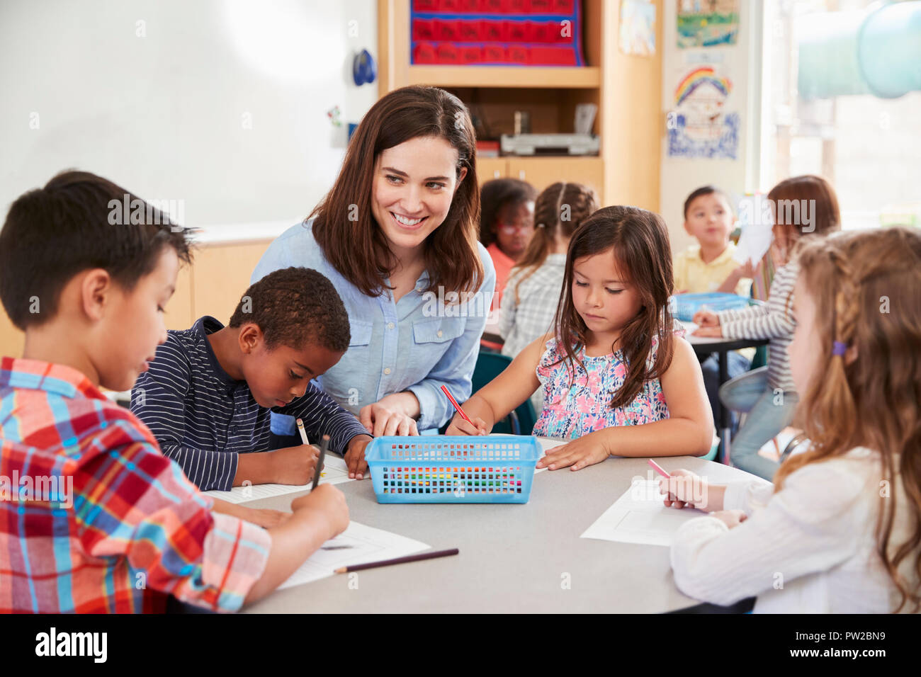 Teacher sitting at table with young school kids in classroom Stock ...