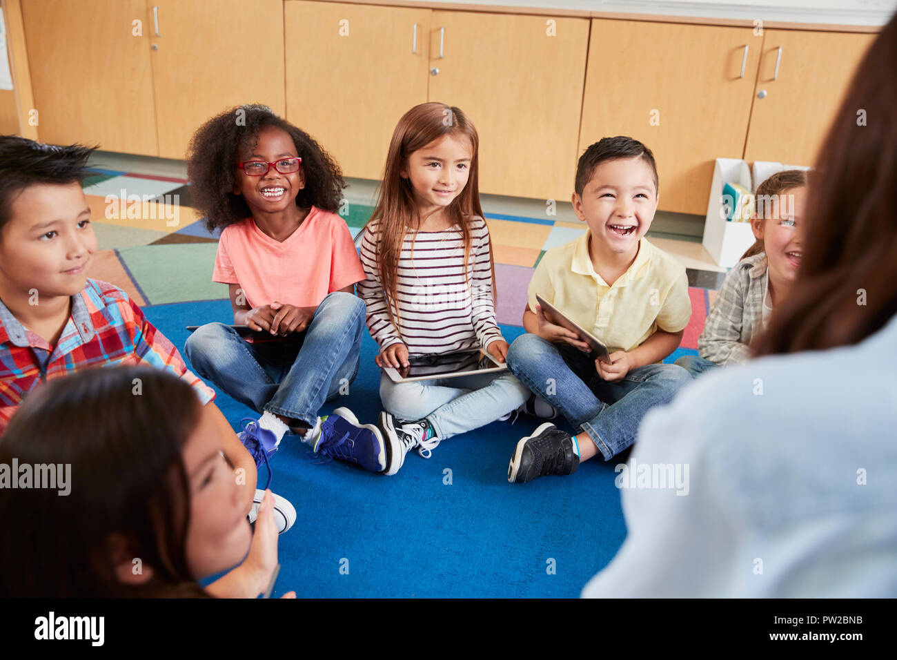 Elementary school kids sitting on floor looking at teacher Stock Photo ...