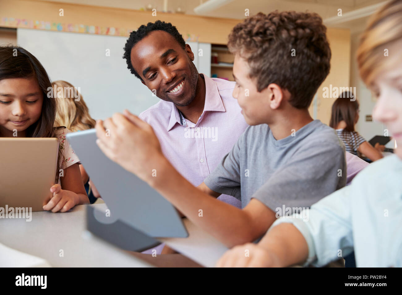 Teacher using tablet computer at desk with school kids Stock Photo - Alamy