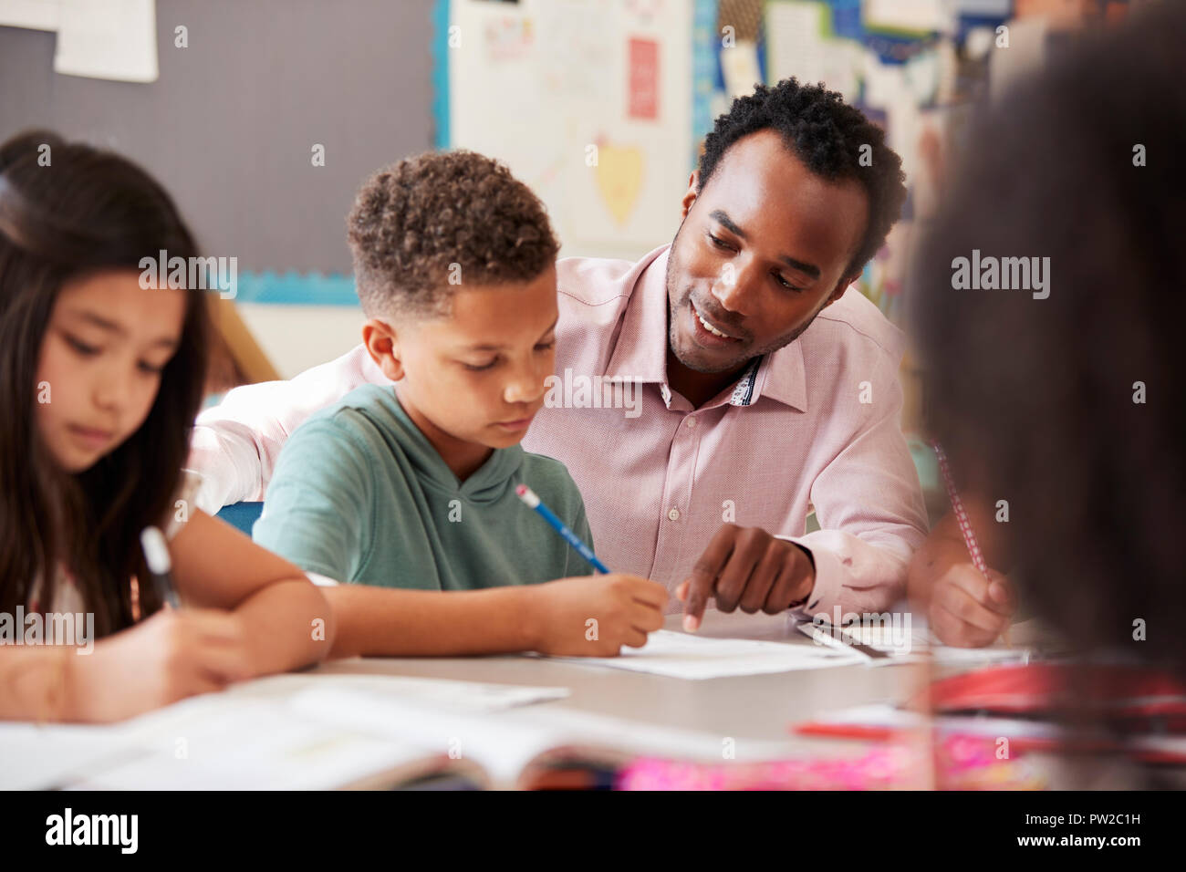 Male teacher working with elementary school boy at his desk Stock Photo ...