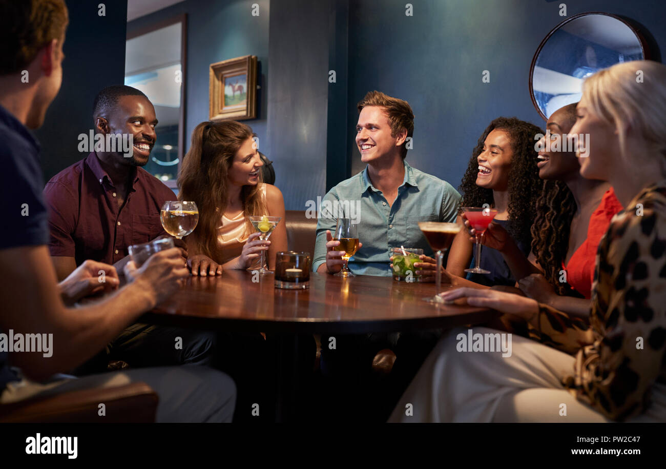 Group Of Young Friends Sitting Around Table In Bar Together On Night ...