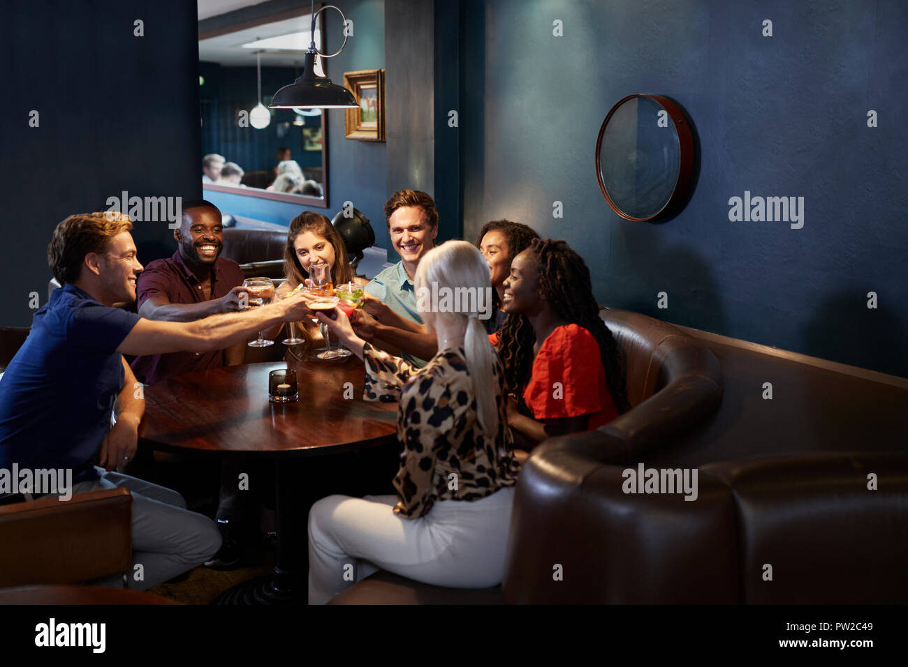 Group Of Young Friends Sitting Around Table And Making A Toast In Bar ...