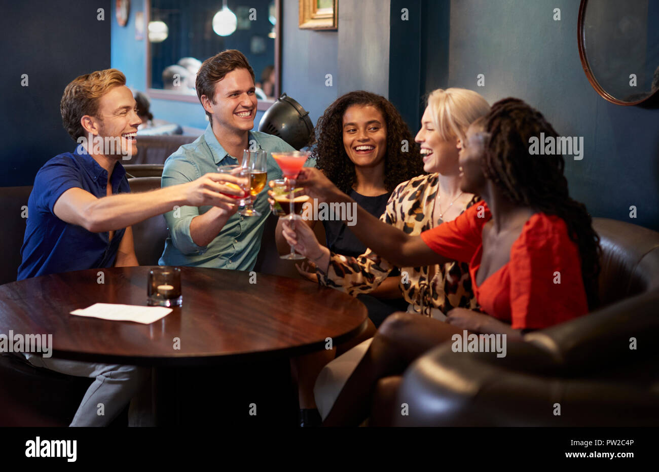 Group Of Young Friends Sitting Around Table And Making A Toast In Bar ...