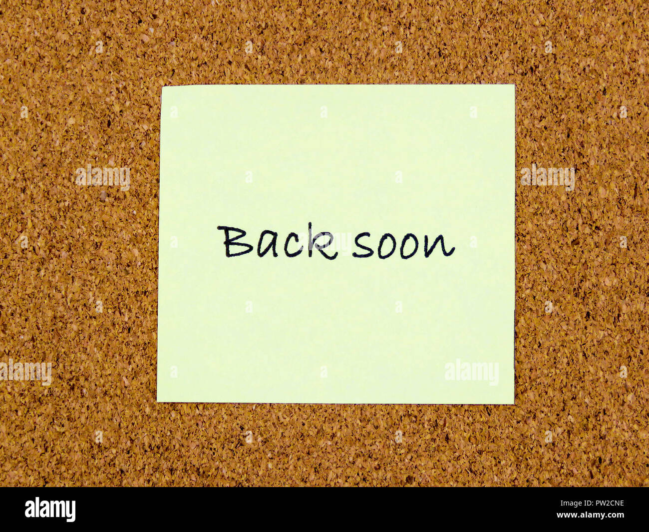 A yellow sticky note with back soon written on it on a cork board ...