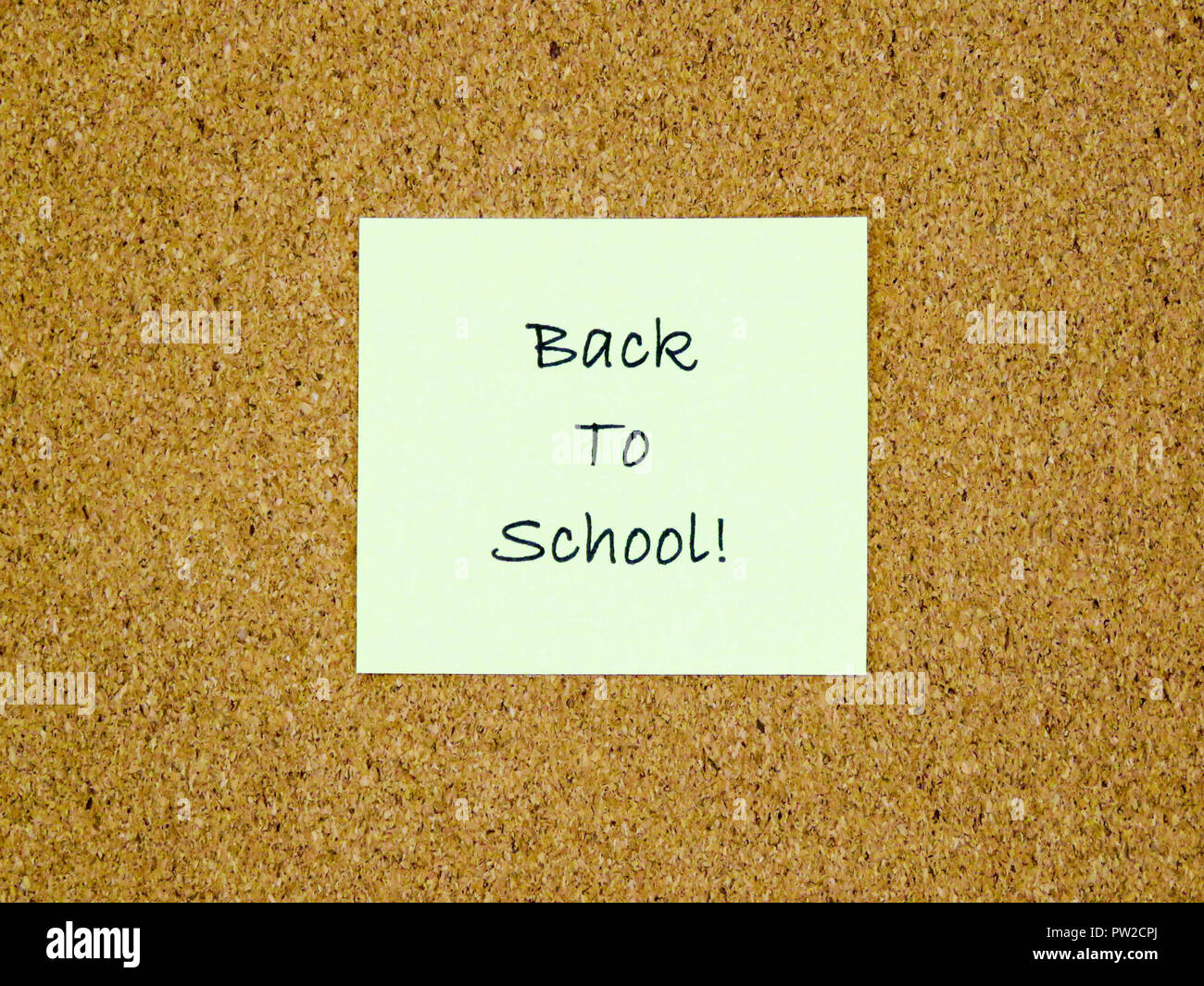 A yellow sticky note with back to school written on it on a cork board ...
