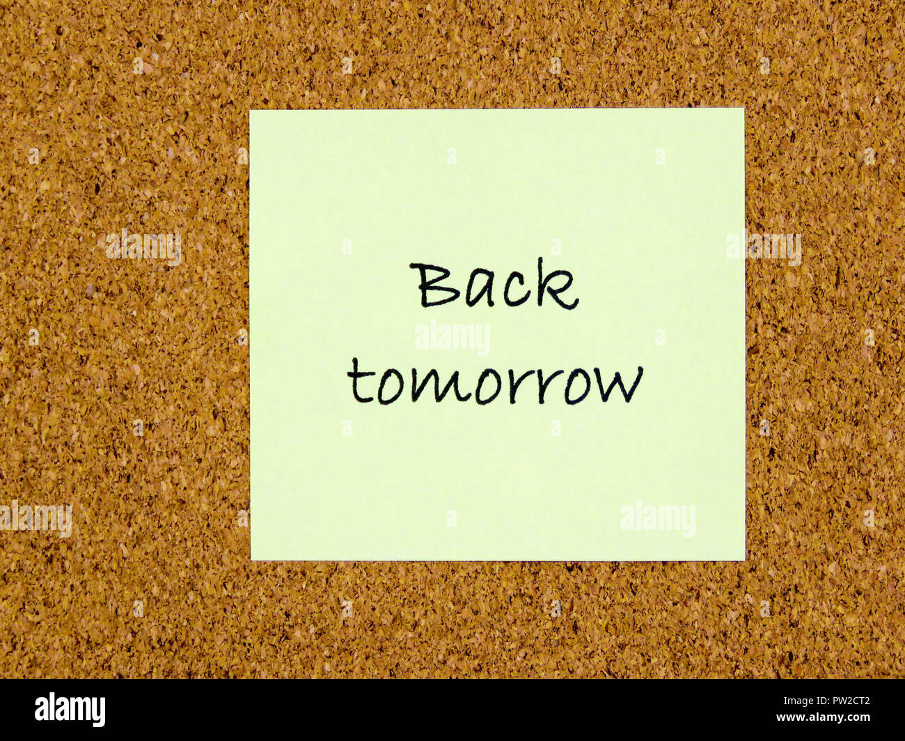 A yellow sticky note with back tomorrow written on it on a cork board ...