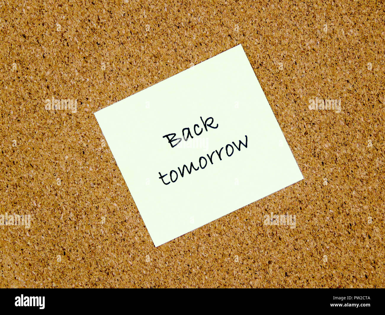 A yellow sticky note with back tomorrow written on it on a cork board ...