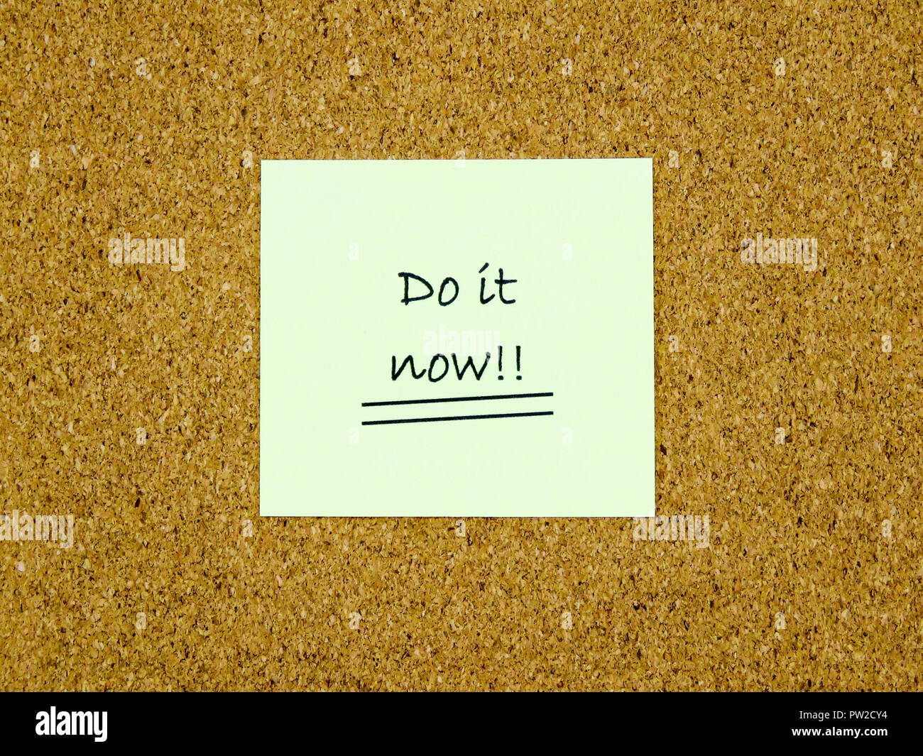 A yellow sticky note with do it now written on it on a cork board ...